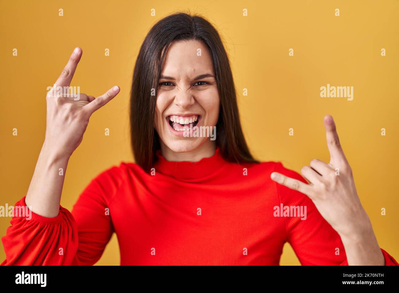 Young hispanic woman standing over yellow background shouting with ...