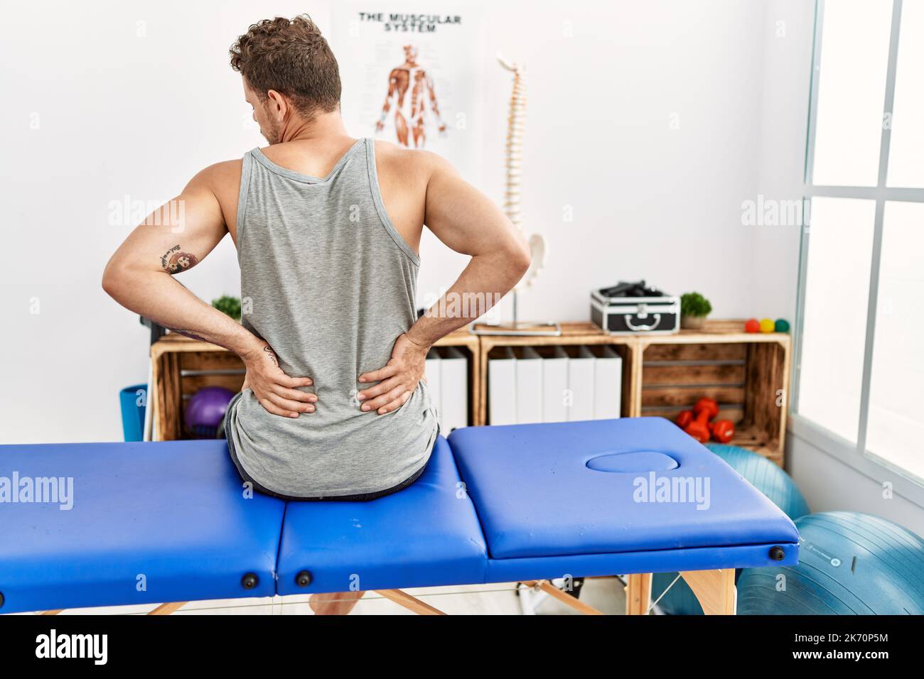 Young hispanic man touching injury back sitting on massage board at ...