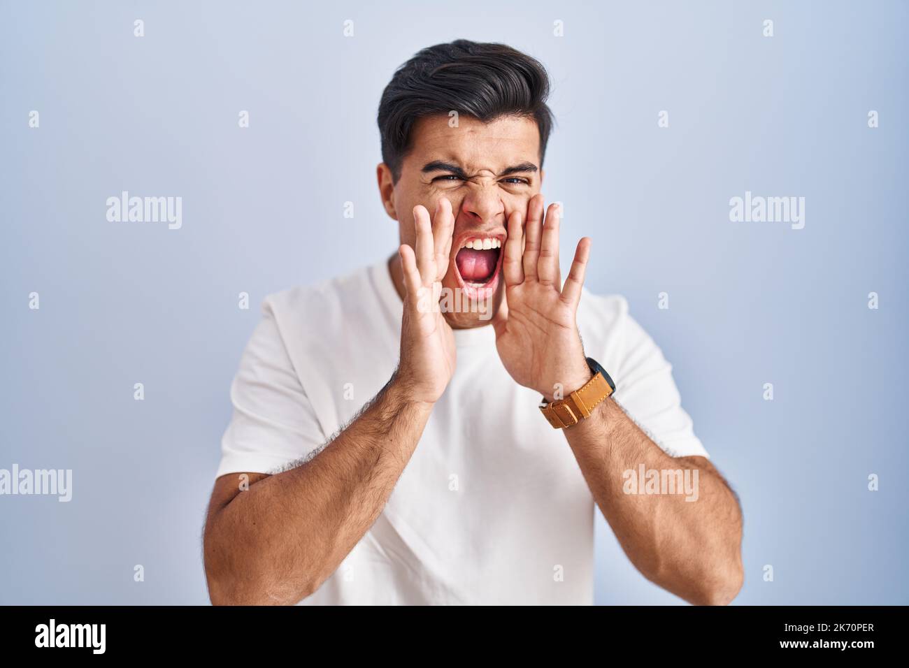 Hispanic man standing over blue background shouting angry out loud with ...