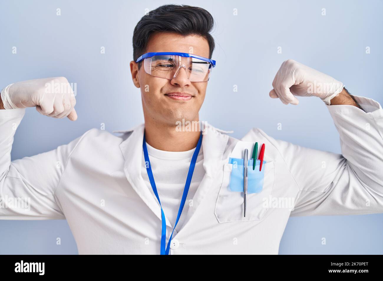 Hispanic man working as scientist showing arms muscles smiling proud ...