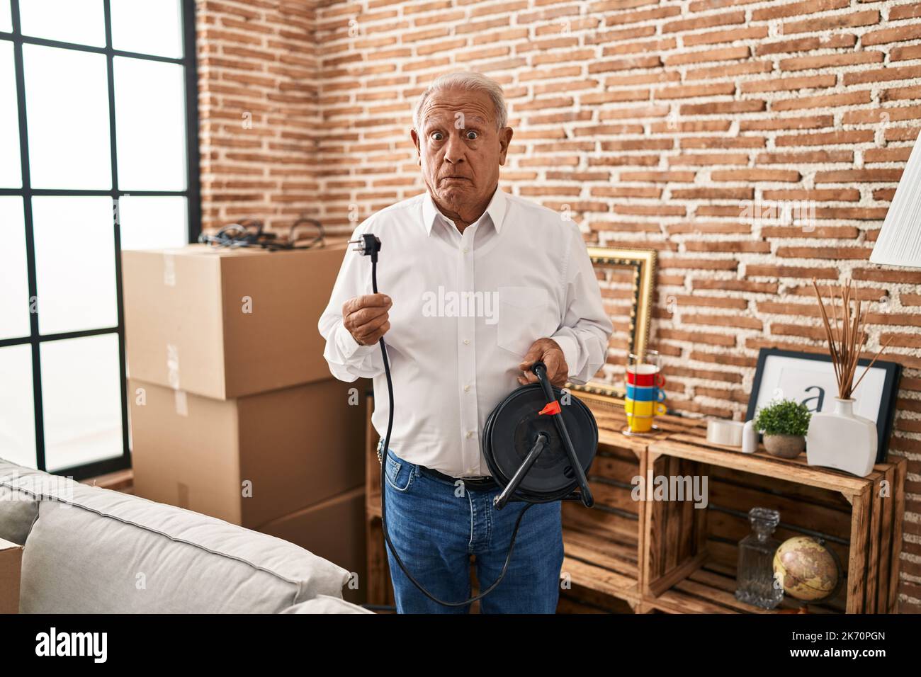 Senior man with grey hair holding extension plug skeptic and nervous ...