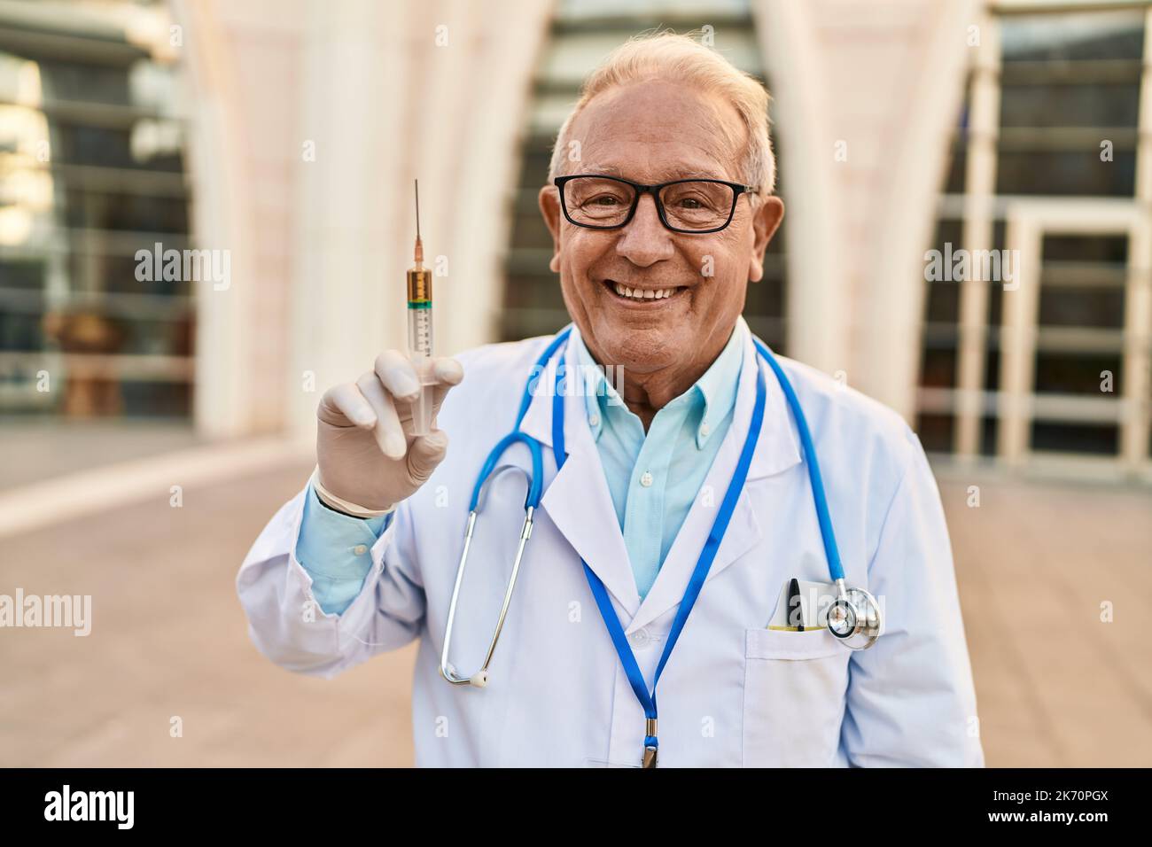 Senior doctor with grey hair holding syringe looking positive and happy ...