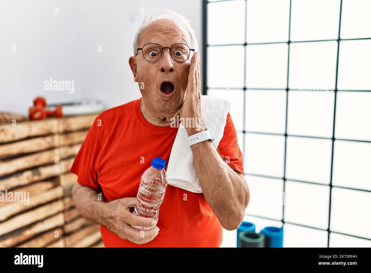 Senior man wearing sportswear and towel at the gym afraid and shocked ...
