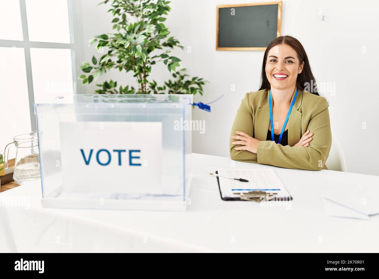 Young brunette woman sitting at election table with voting ballot happy ...