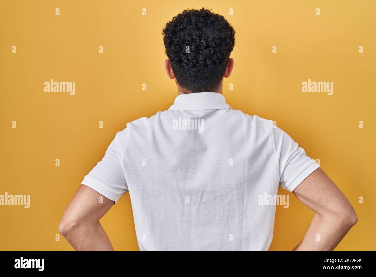 Arab man standing over yellow background standing backwards looking ...