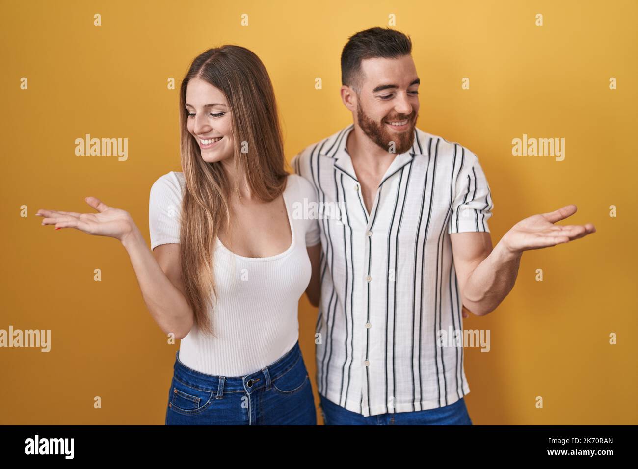 Young couple standing over yellow background smiling showing both hands ...