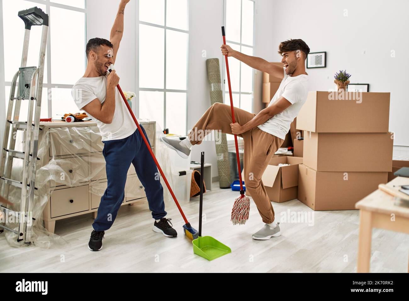 Two hispanic men couple cleaning and dancing at new home Stock Photo ...