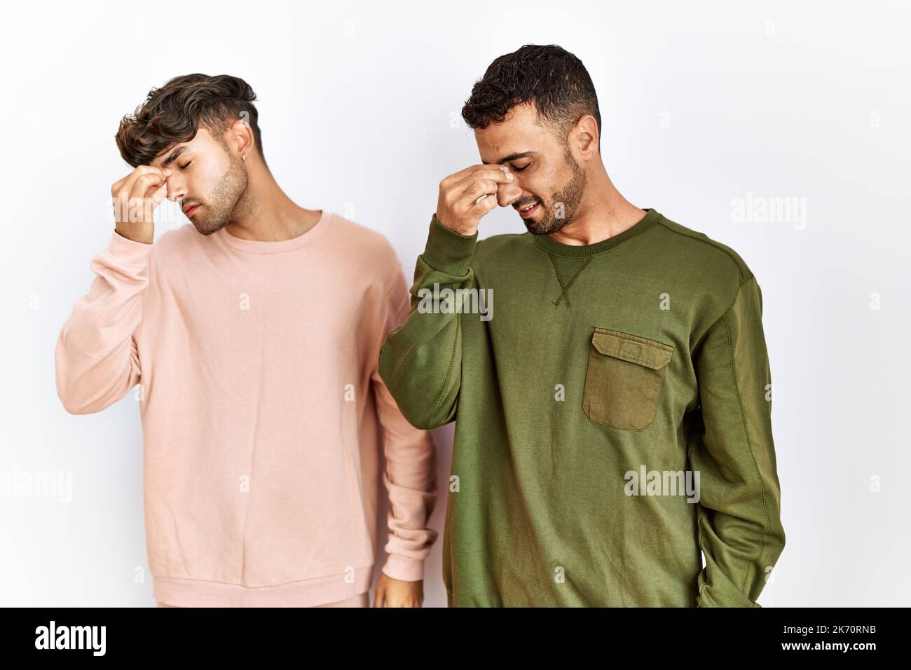Young gay couple standing over isolated white background tired rubbing ...