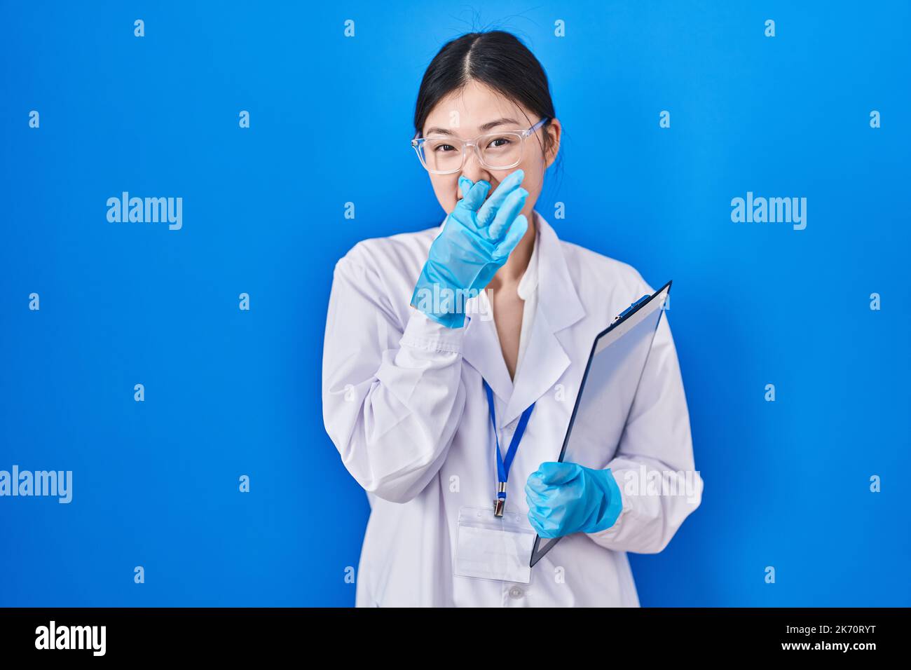 Chinese young woman working at scientist laboratory smelling something ...
