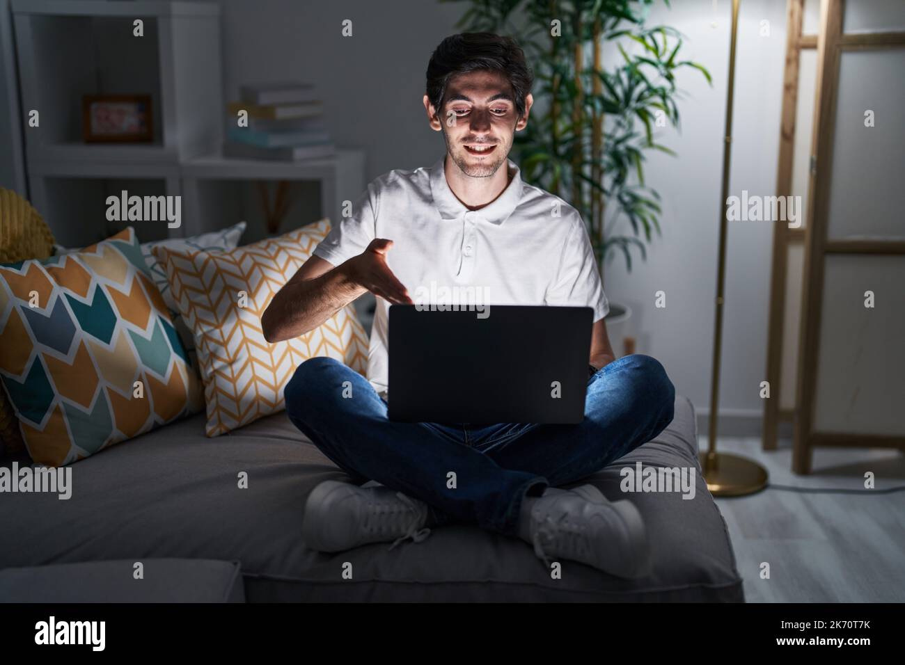 Young hispanic man using laptop at home at night smiling friendly ...