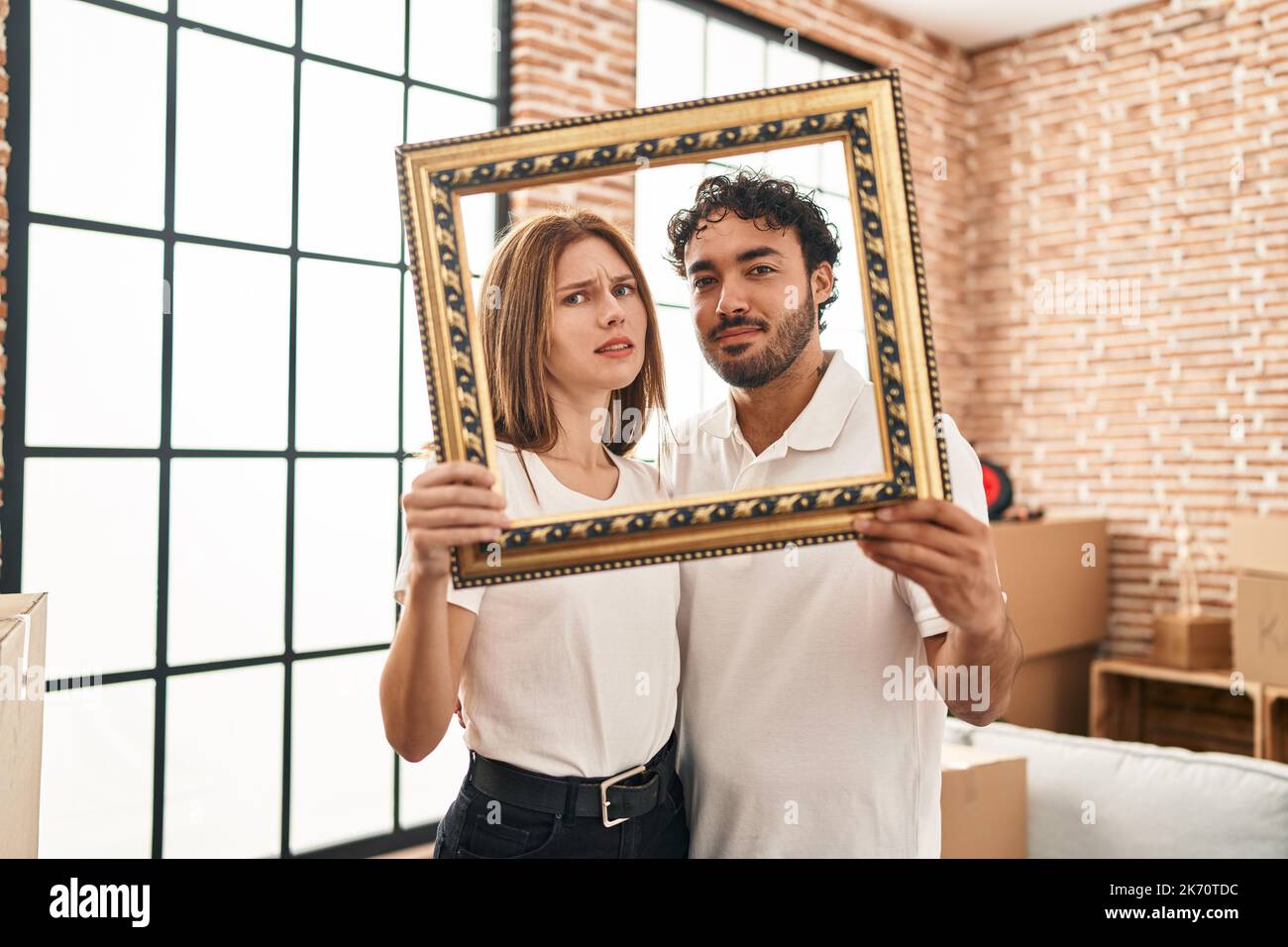 Young two people holding empty frame together clueless and confused ...