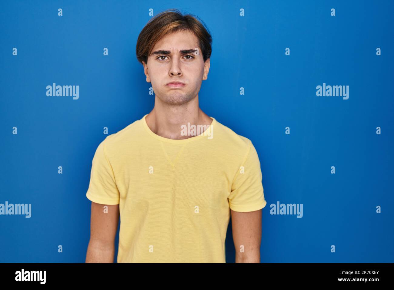 Young man standing over blue background puffing cheeks with funny face ...