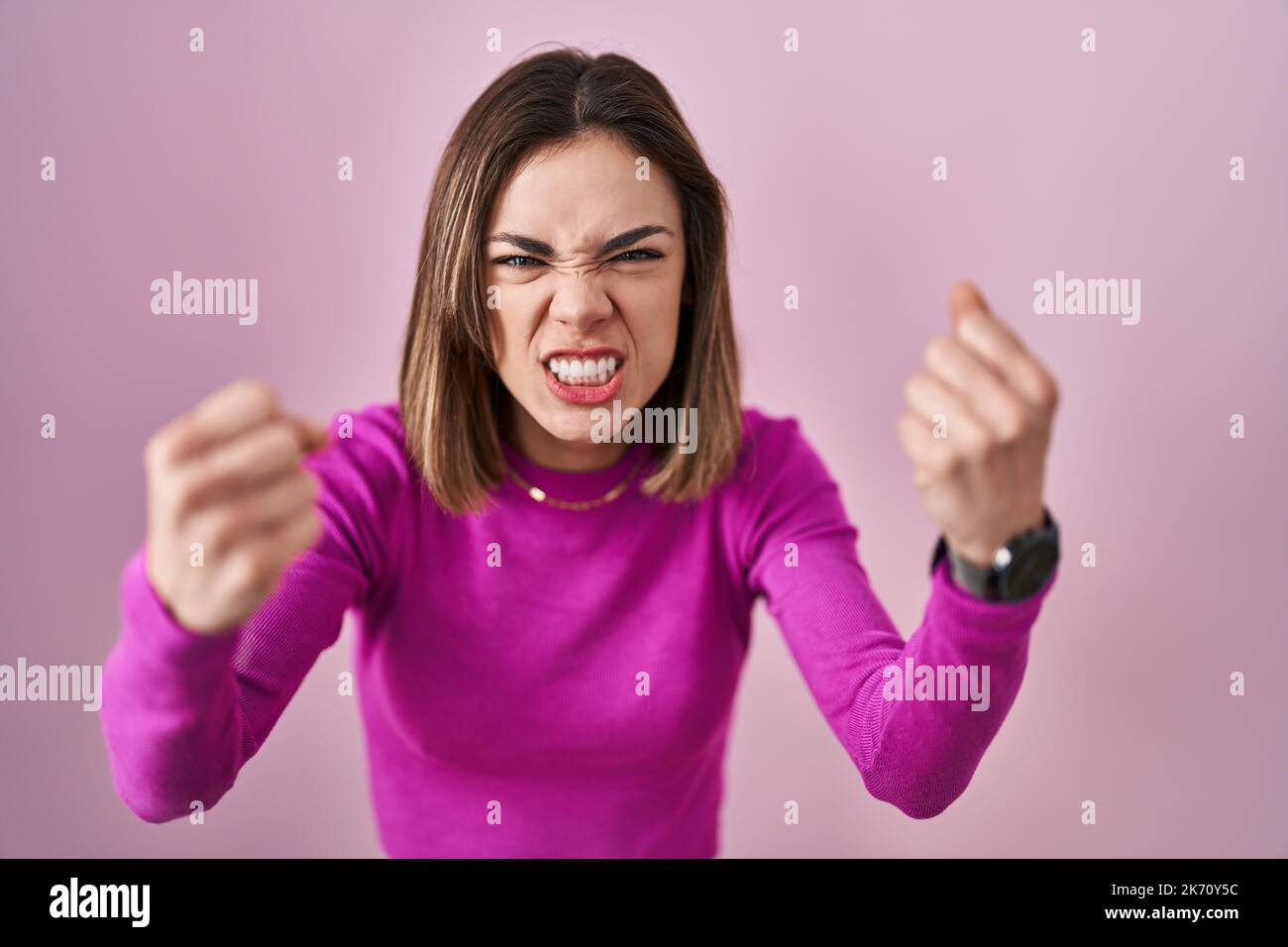 Hispanic woman standing over pink background angry and mad raising ...