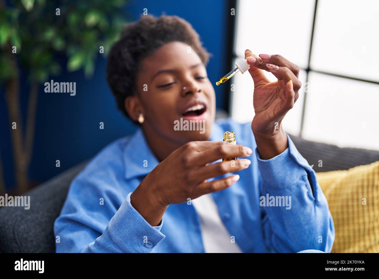 African american woman taking medical syrup sitting on sofa at home ...