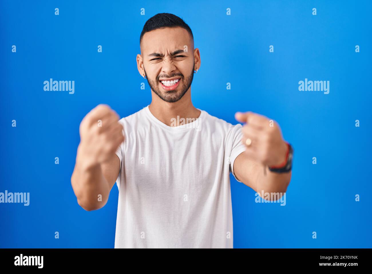 Young hispanic man standing over blue background angry and mad raising ...
