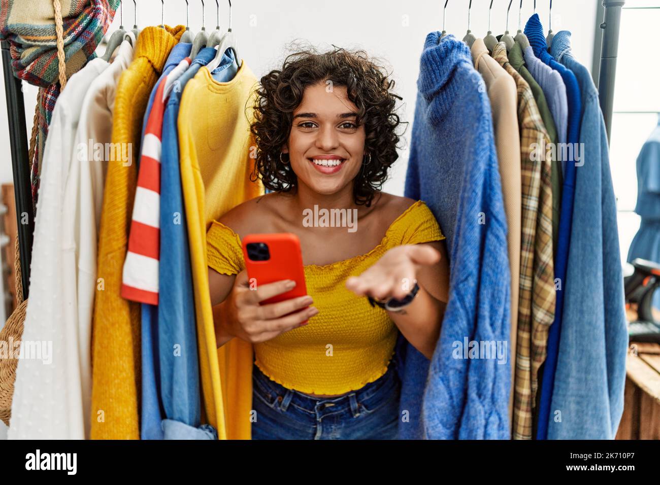 Young hispanic woman searching clothes on clothing rack using ...