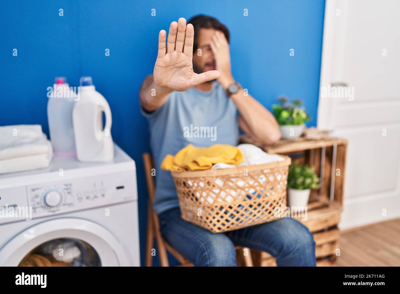 Handsome middle age man waiting for laundry covering eyes with hands ...