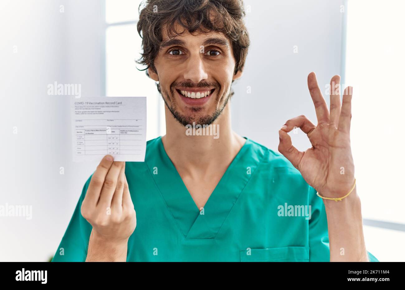 Young hispanic doctor man holding covid record card smiling positive ...