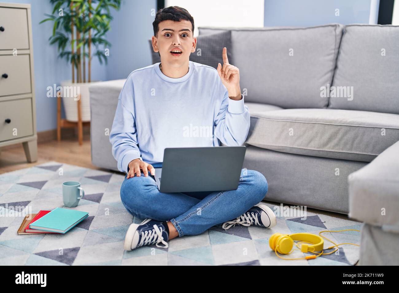 Non binary person studying using computer laptop sitting on the floor ...