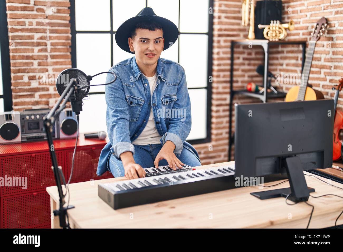Young non binary man musician playing piano keyboard at music studio ...