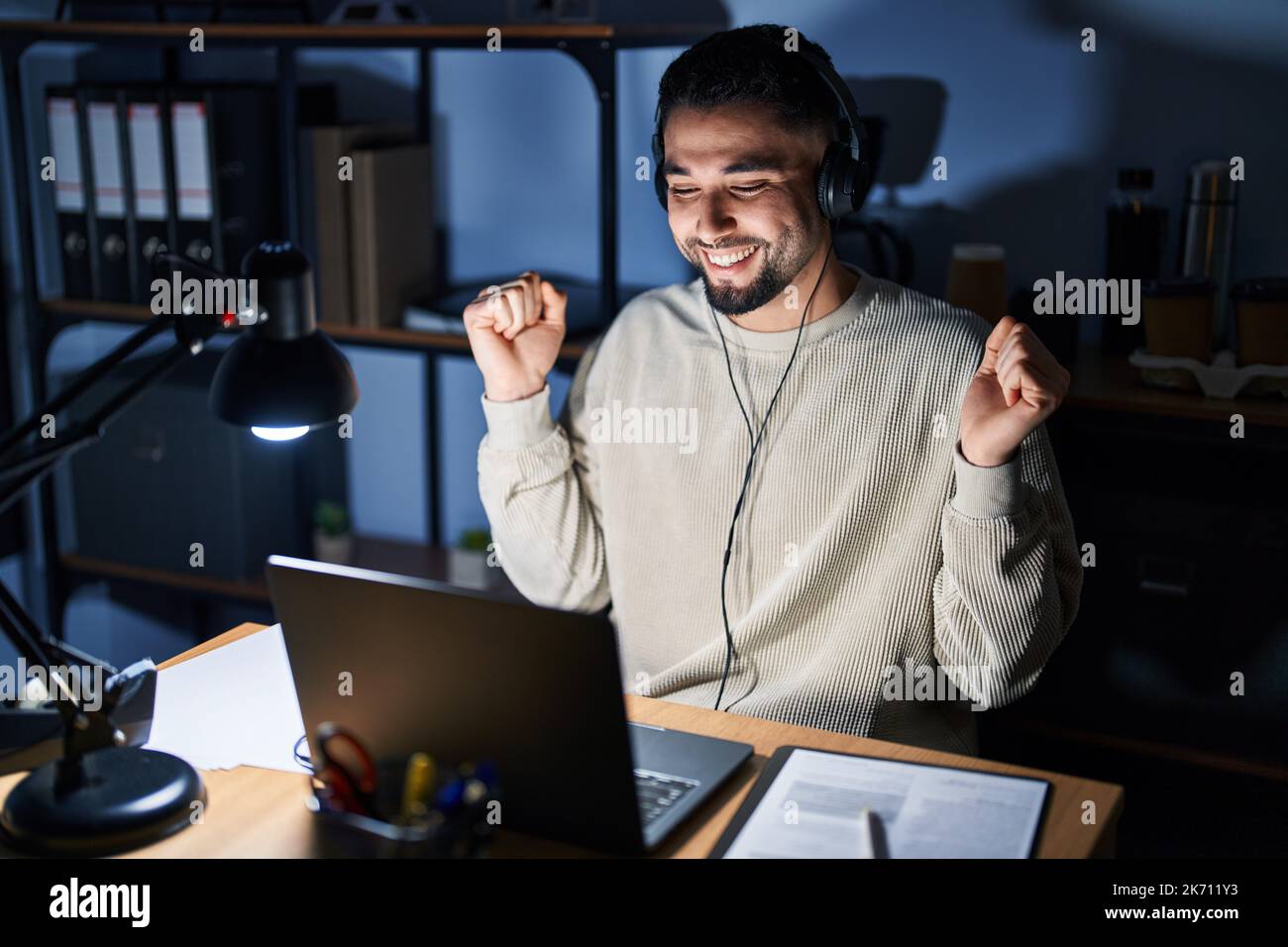 Young handsome man working using computer laptop at night celebrating ...