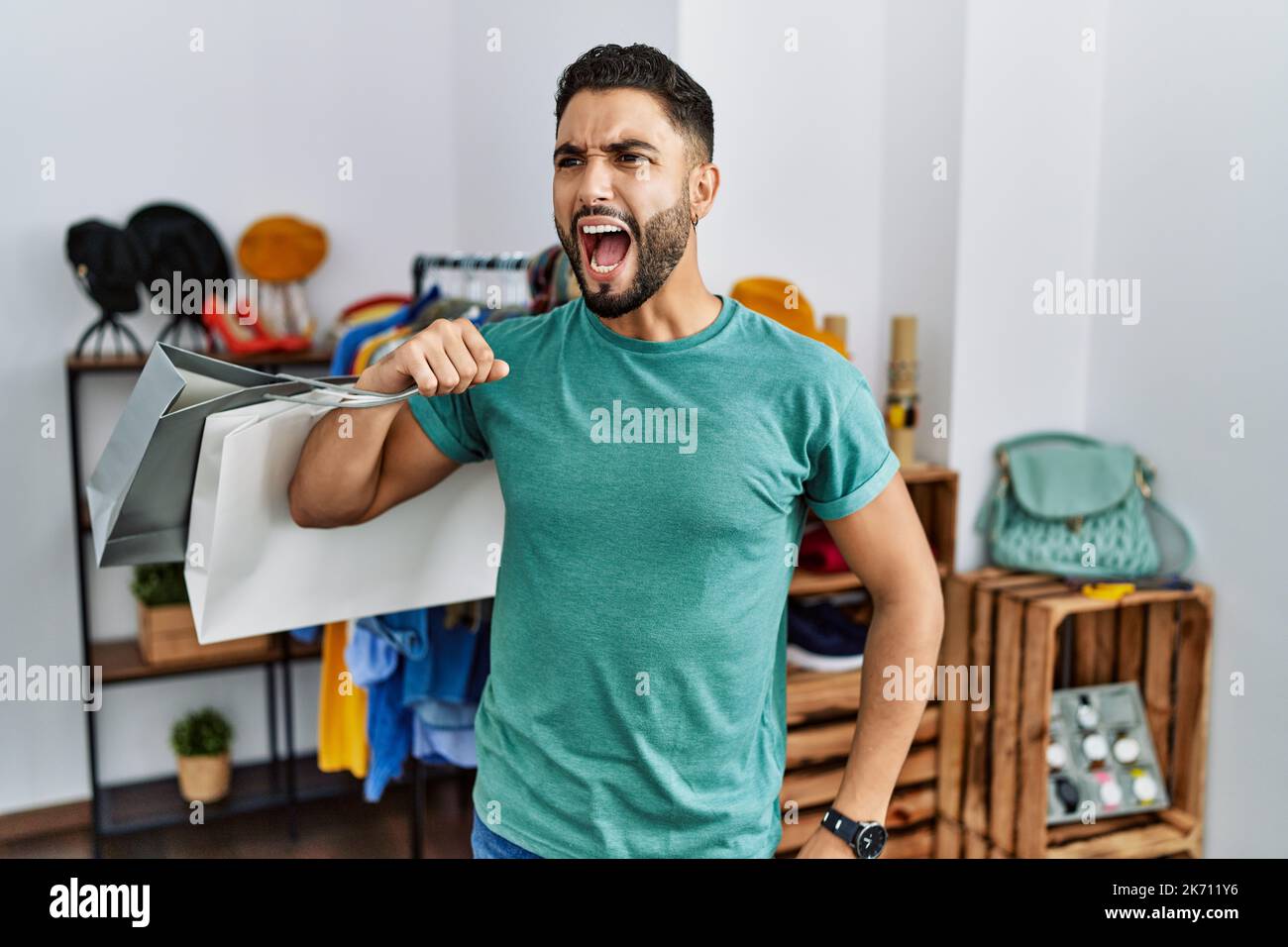 Young handsome man with beard holding shopping bags at retail shop ...