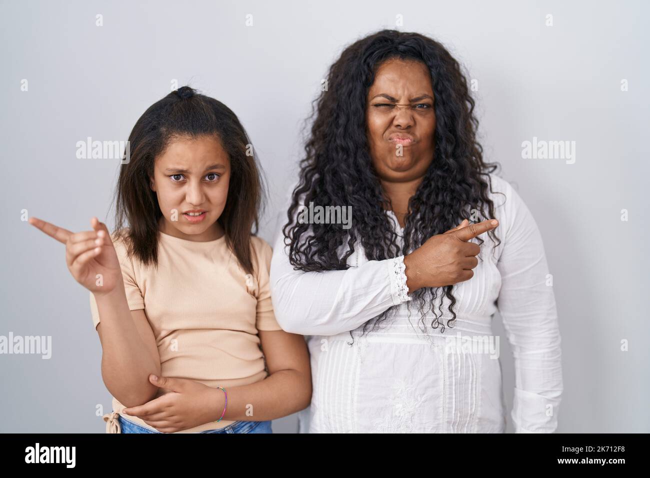 Mother and young daughter standing over white background pointing aside ...