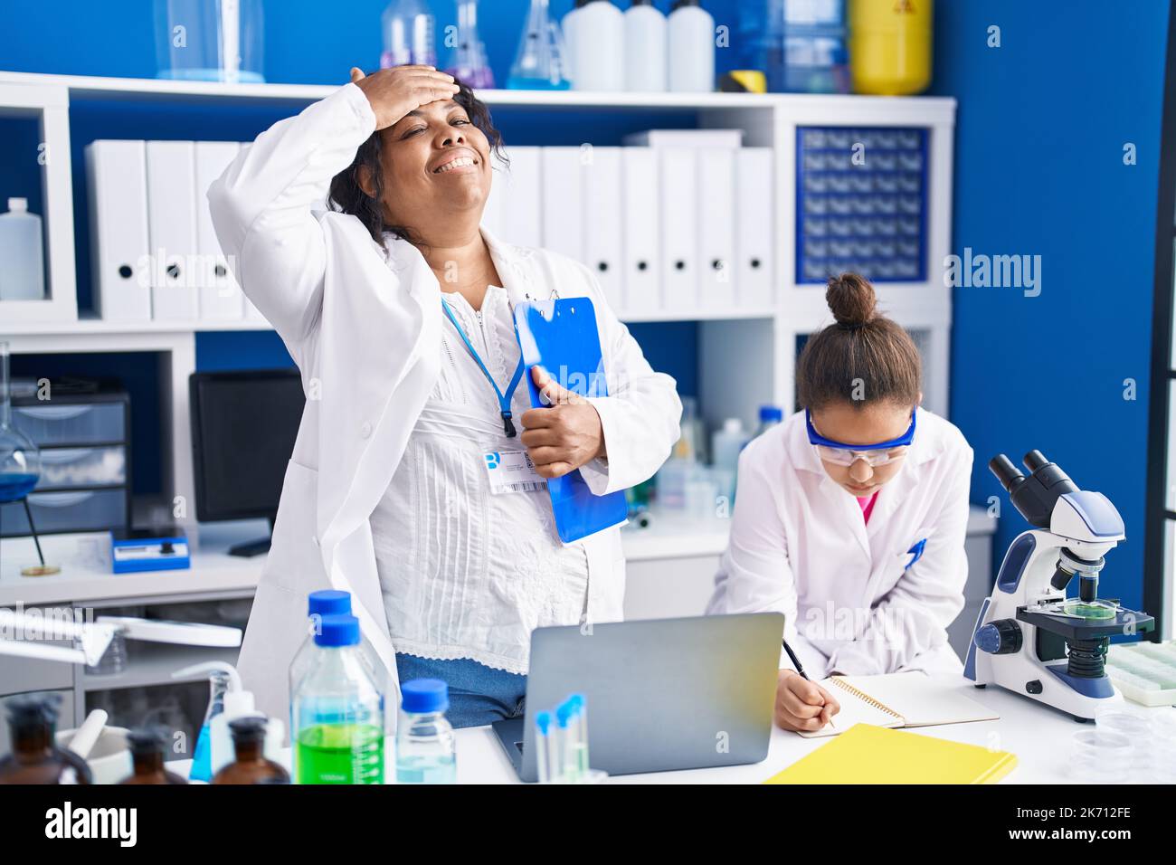 Mother and young daughter working at scientist laboratory stressed and ...