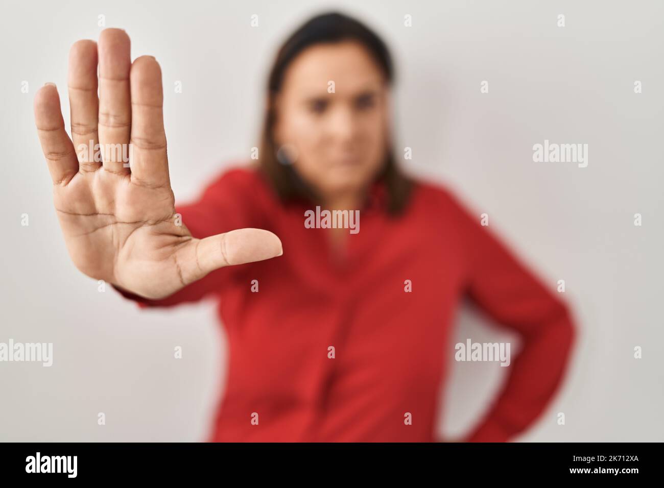 Hispanic mature woman standing over white background doing stop sing ...