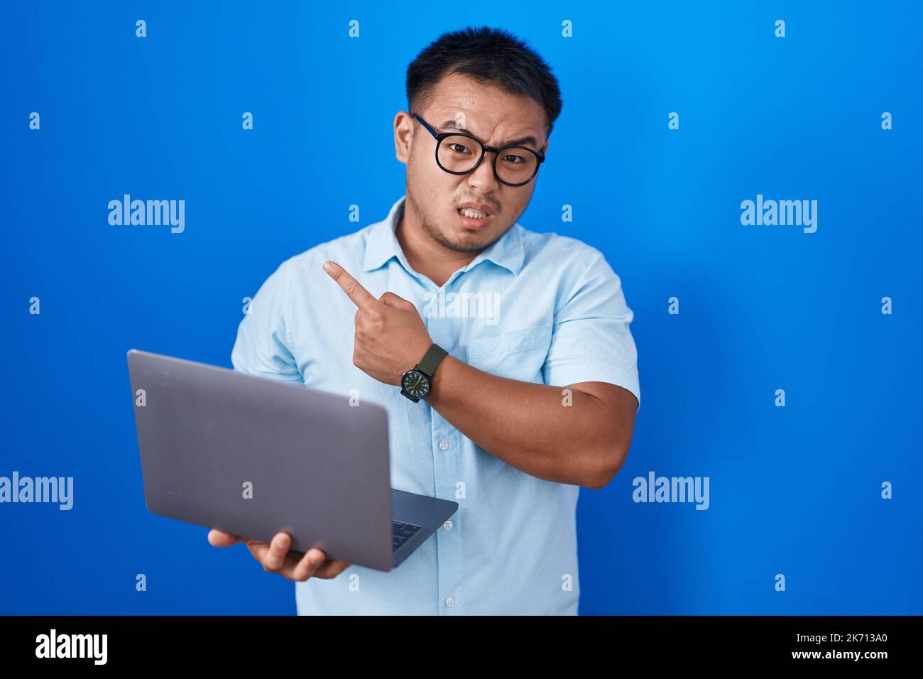 Chinese young man using computer laptop pointing aside worried and ...
