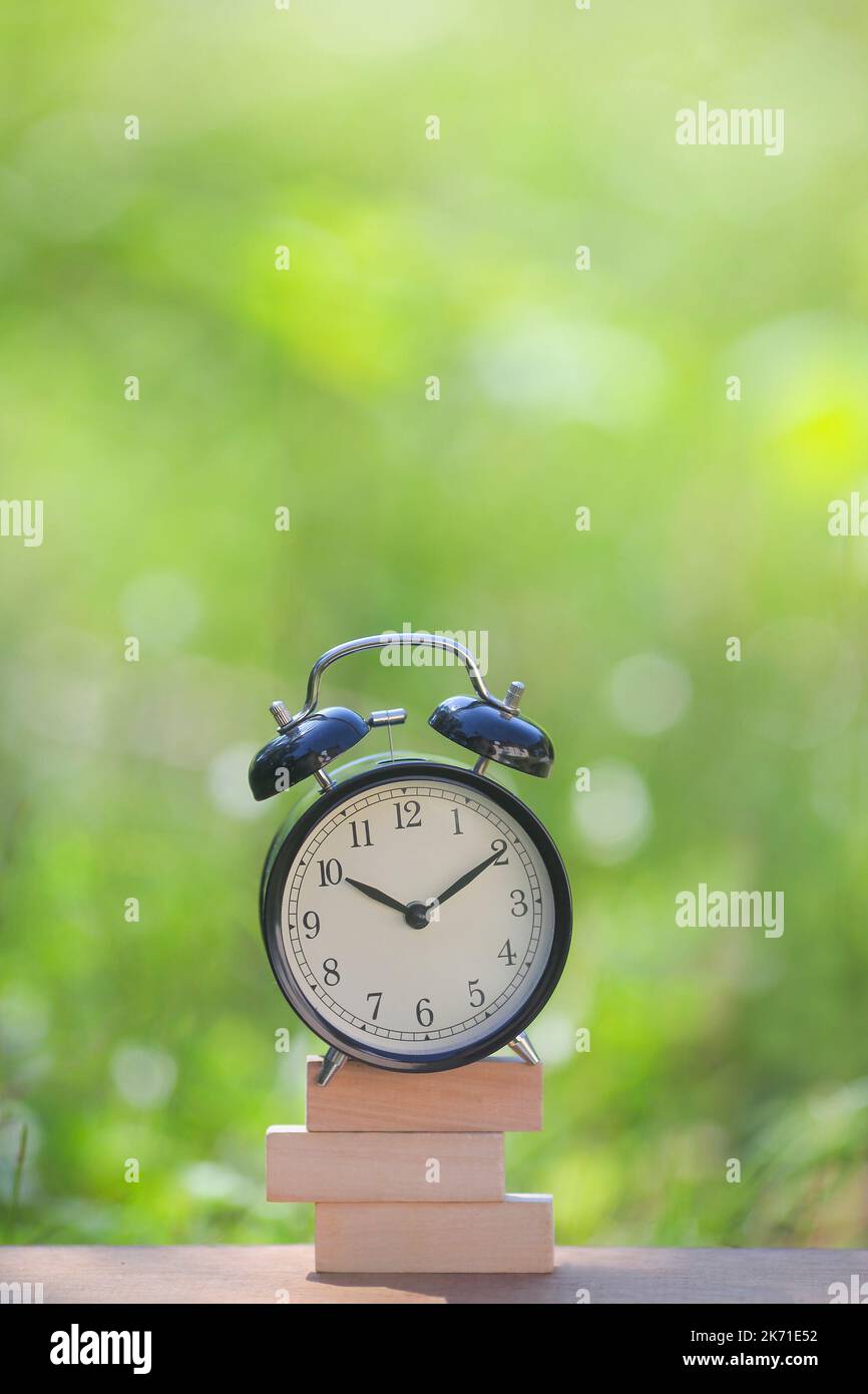 Black alarm clock stacked on wooden bar with shallow DOF green ...