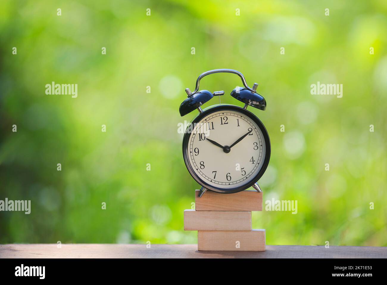 Black alarm clock stacked on wooden bar with shallow DOF green ...