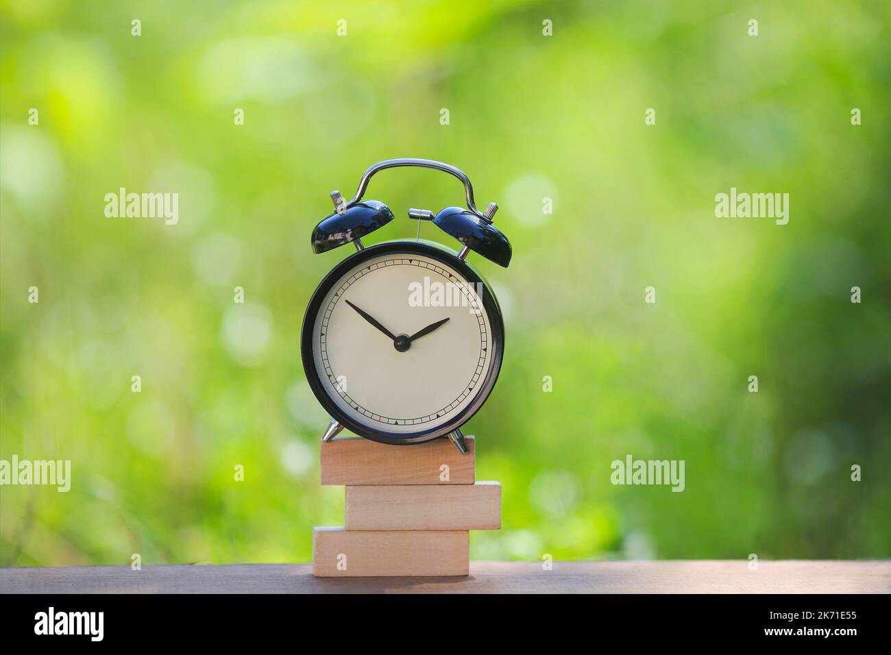 Black alarm clock stacked on wooden bar with shallow DOF green ...