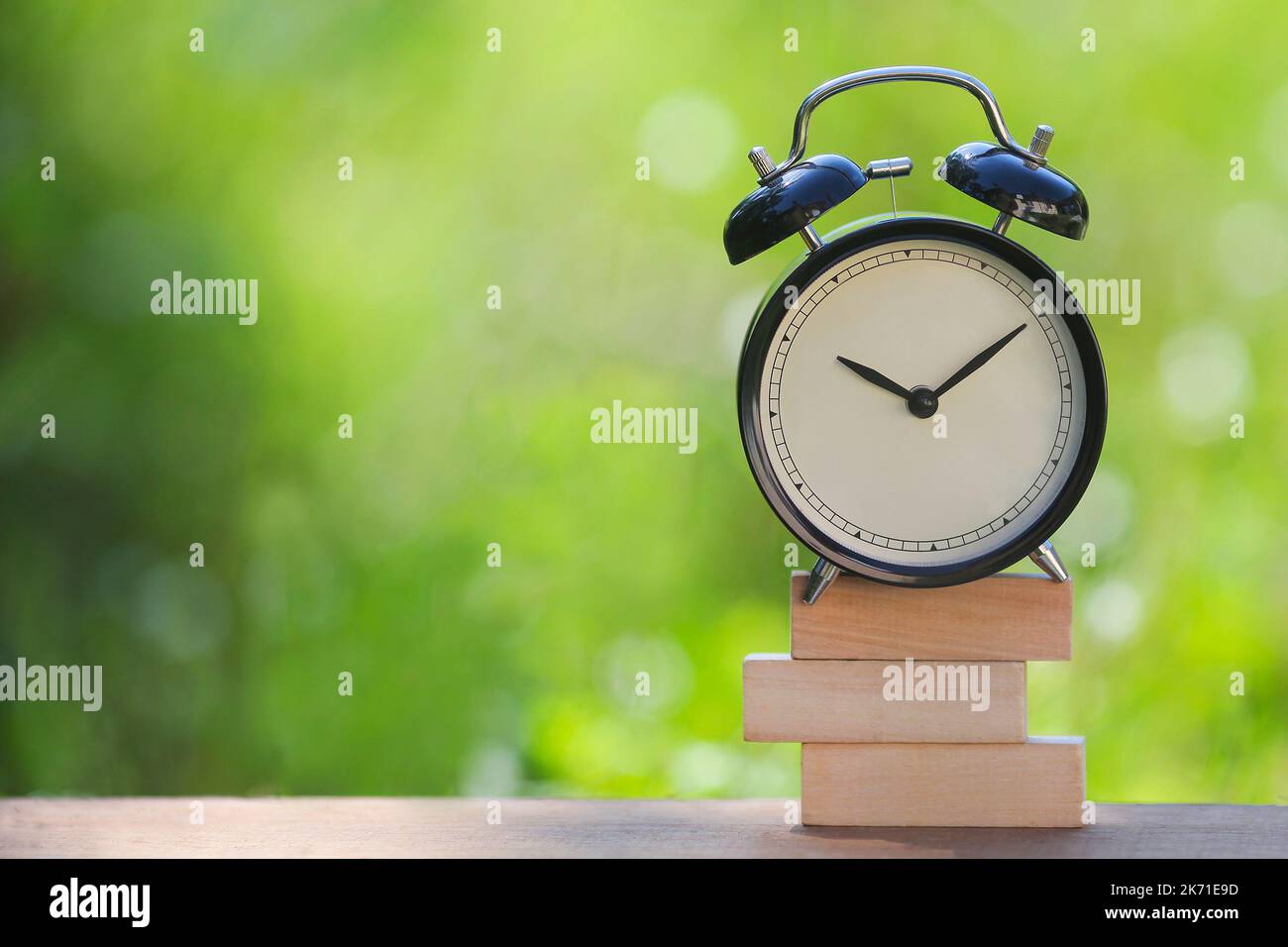 Black alarm clock stacked on wooden bar with shallow DOF green ...