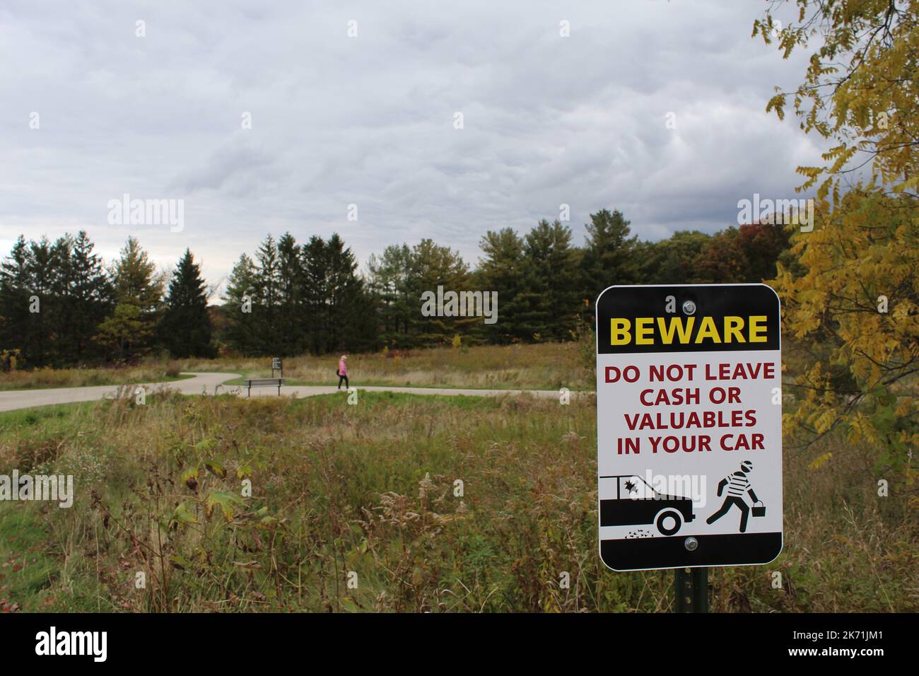 Sign reads Beware Do Not Leave Cash or Valuables in Your Car with woman ...