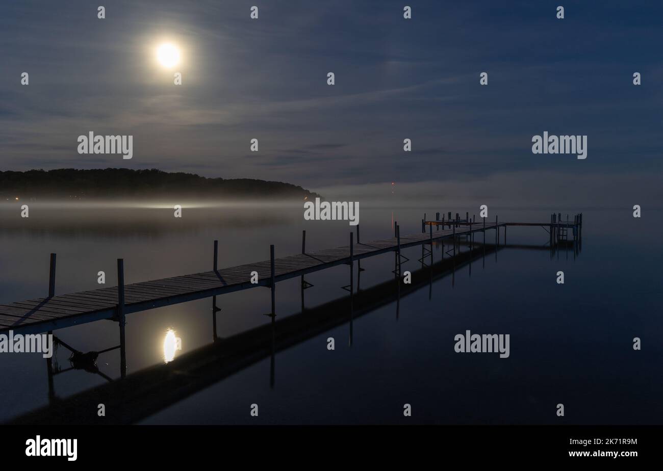 Fog over a lake with a dock in the foreground lit by a full moon Stock ...