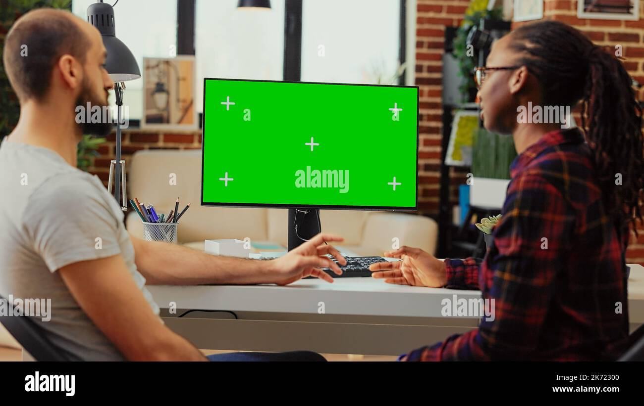 Diverse team working on computer with greenscreen at desk, using monitor to examine isolated ...