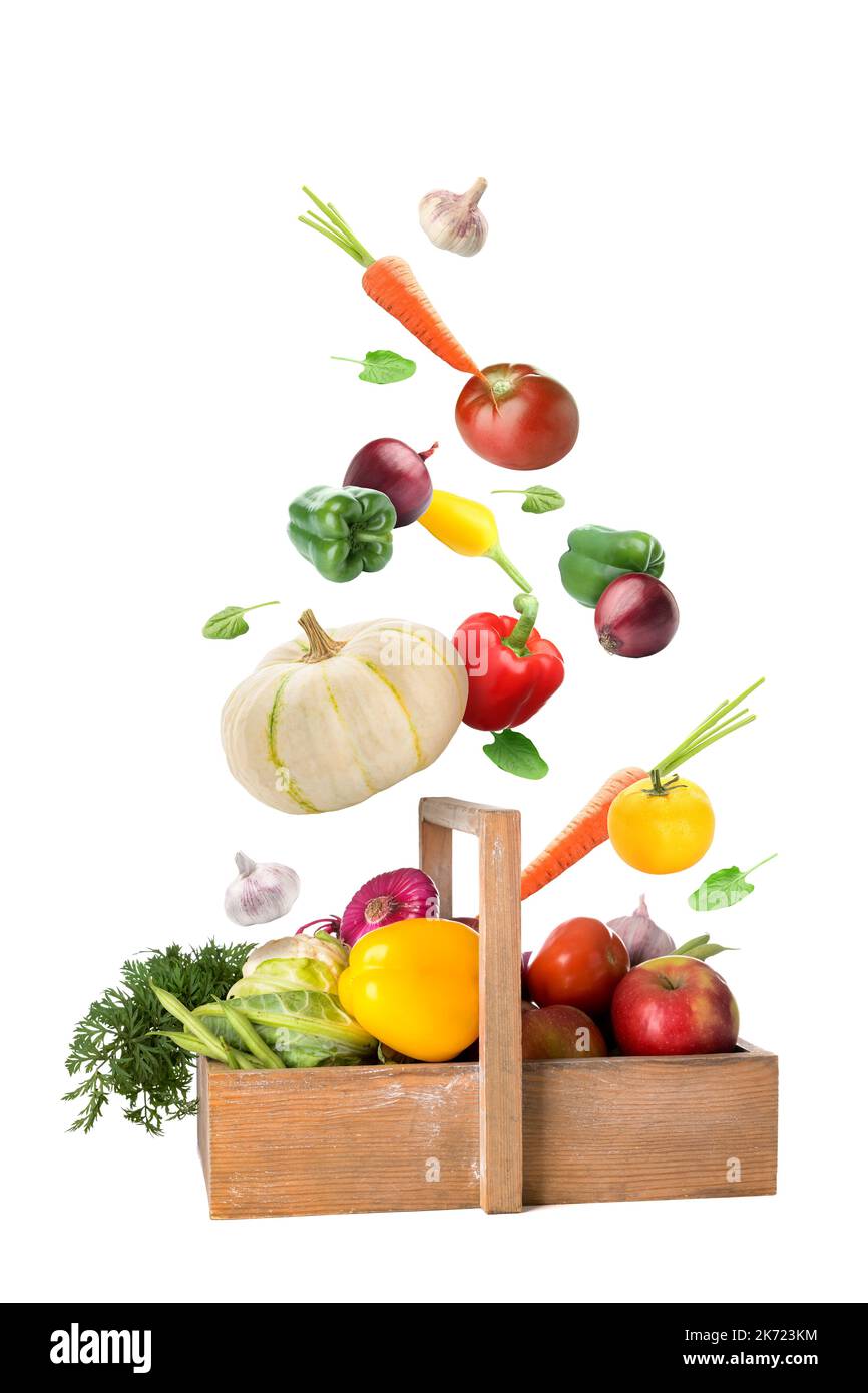 Many healthy vegetables falling into wooden basket on white background ...