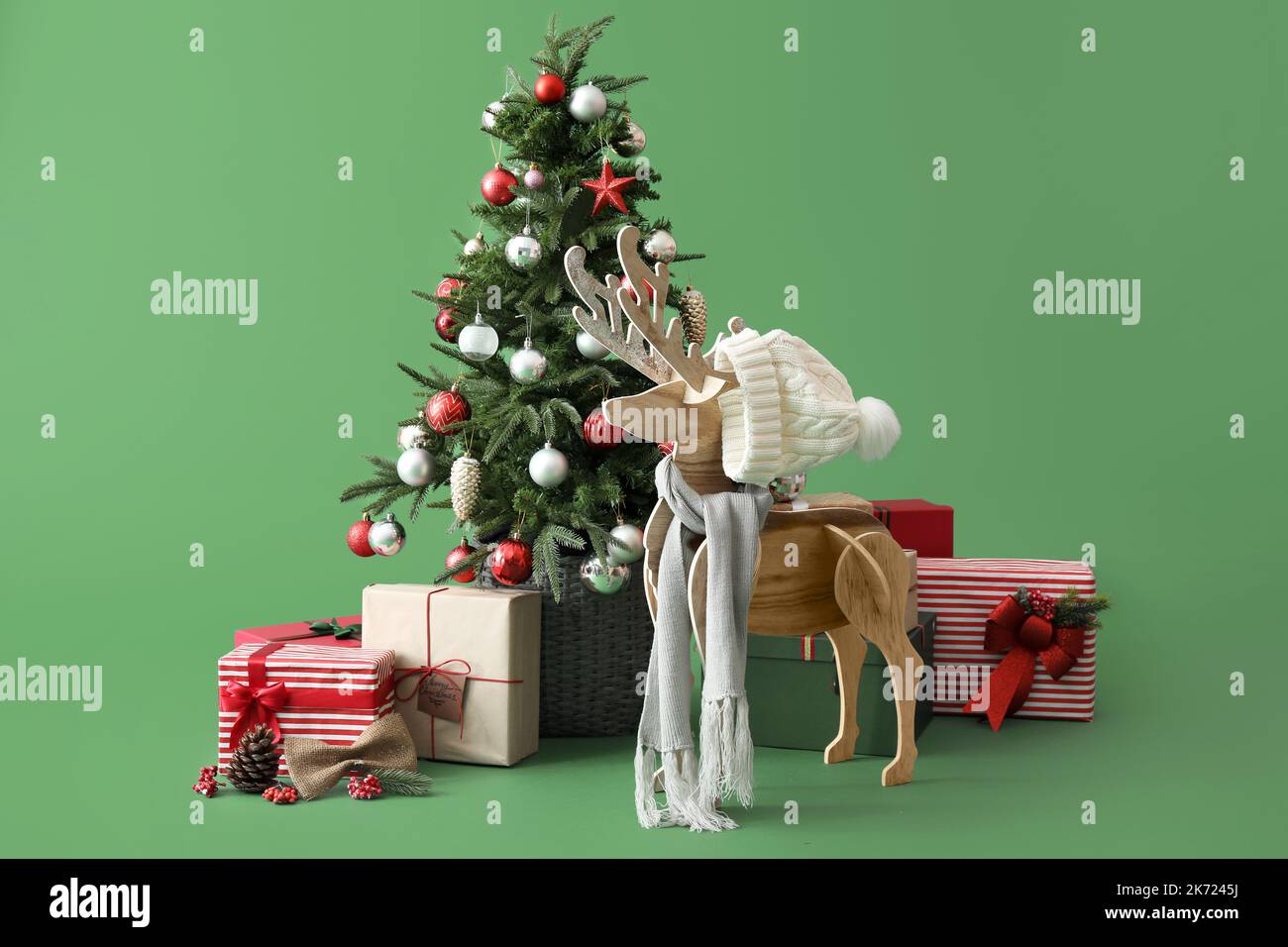 Wooden reindeer with scarf, hat, Christmas tree and presents on green ...