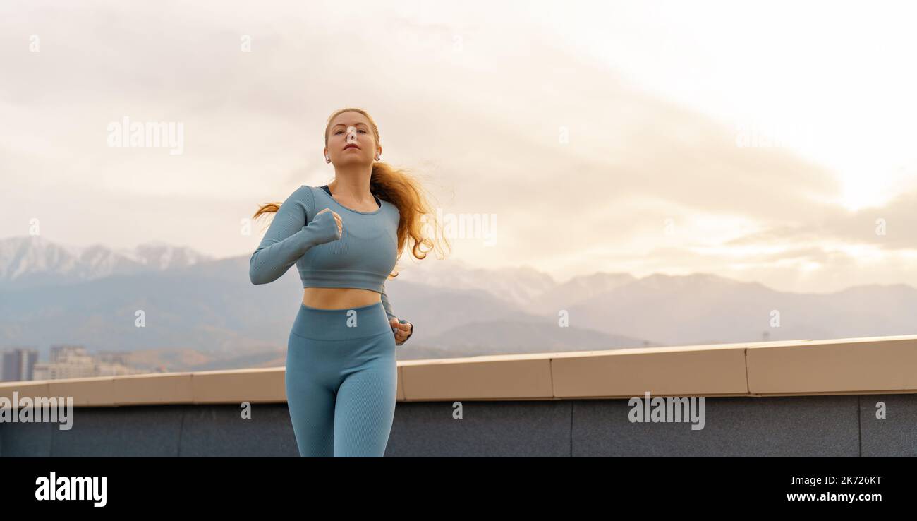 Athletic woman is running on rooftop of parking, garage on sunset ...