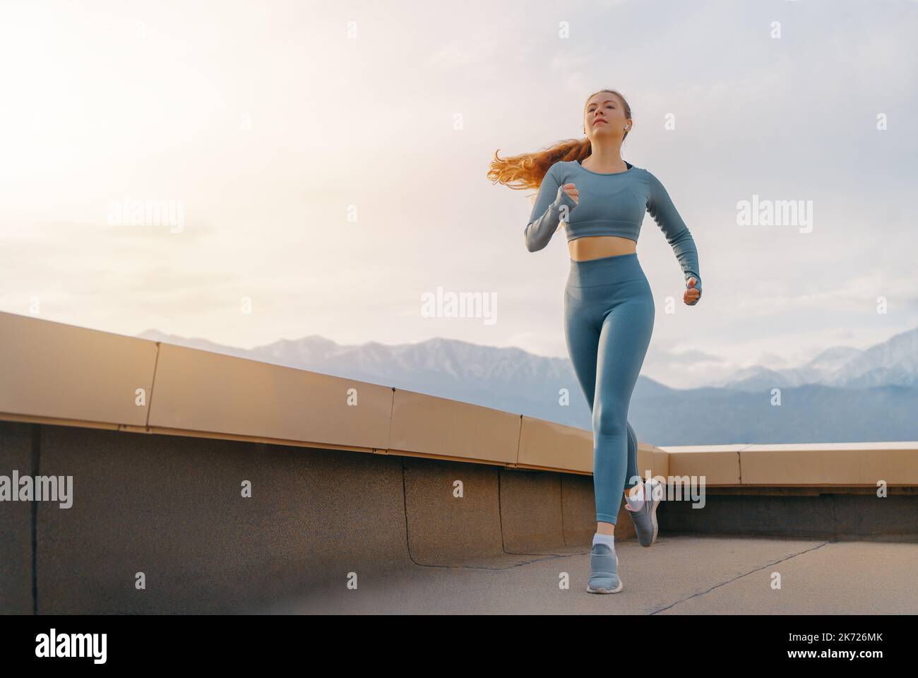 Athletic woman is running on rooftop of parking, garage on sunset ...