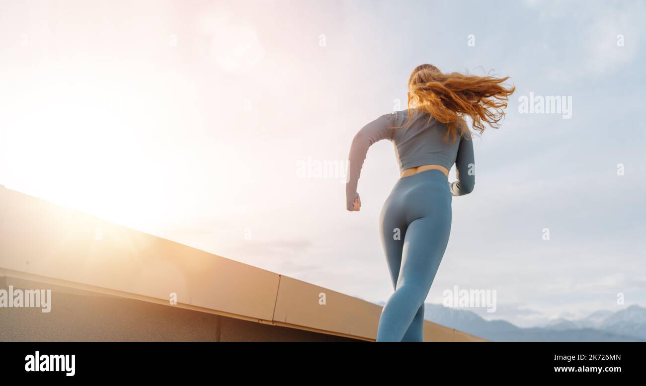 Athletic woman is running on rooftop of parking, garage on sunset ...