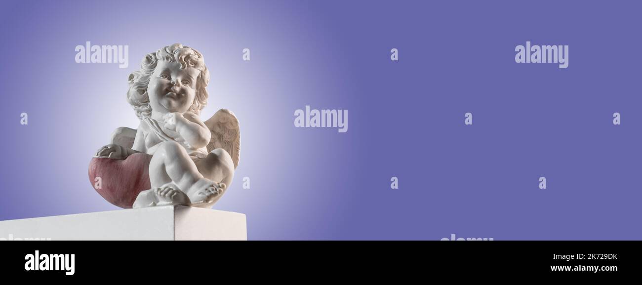 Figurine of an angel Cupid on the podium with a red heart on a very ...