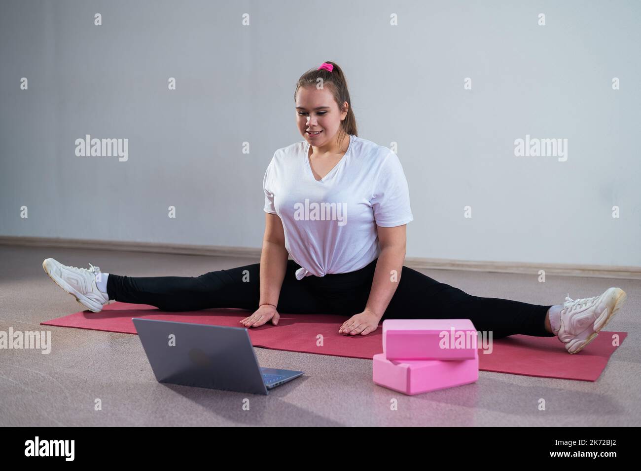 Young caucasian fat woman doing bends on a sports mat and watching a ...