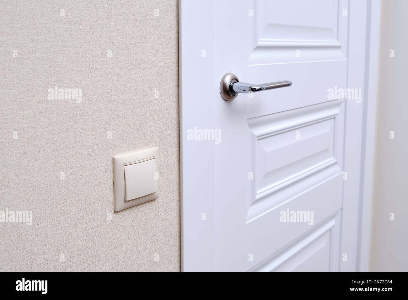 A white door in the home room and a light switch. Metal door handle and ...