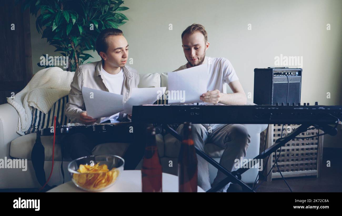 Guitarist and keyboarder are talking looking at music sheet and ...