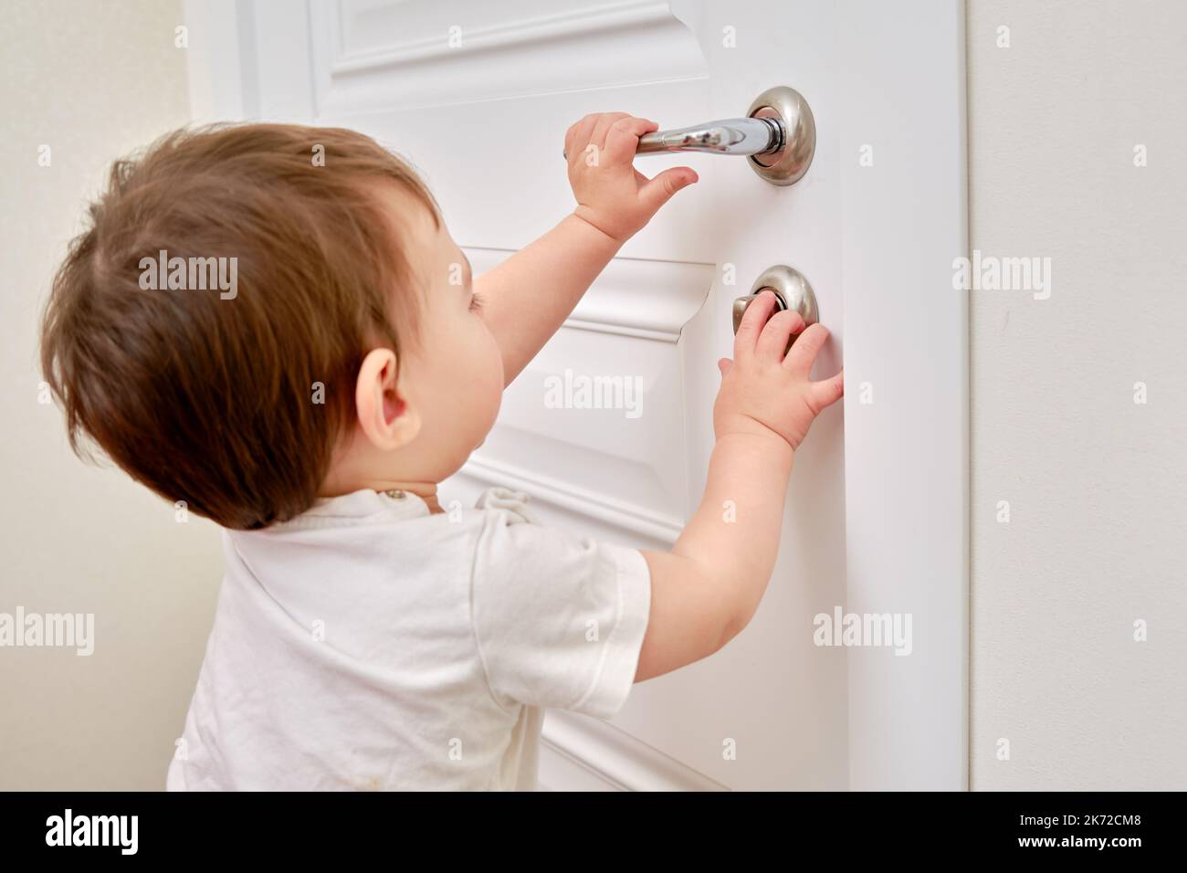 Toddler baby opens the lock, holding the door handle, child hand close ...