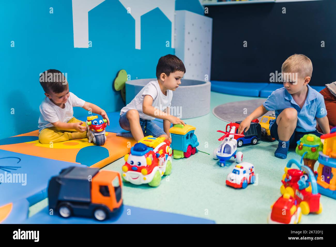 three Caucasian preschoolers playing with the car, train and truck toys ...