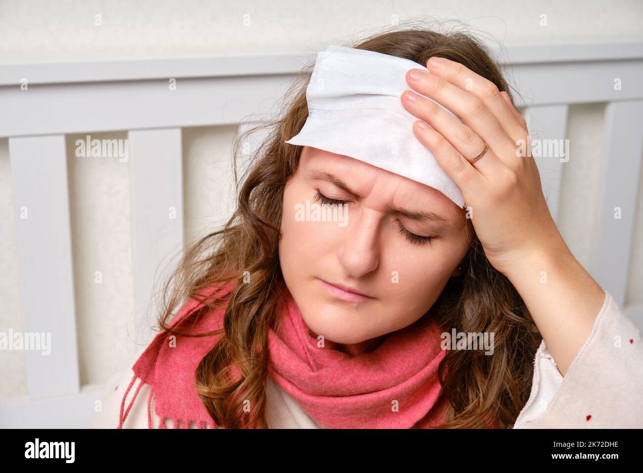 A sick woman applies a wet compress to her head, a hand with a napkin ...