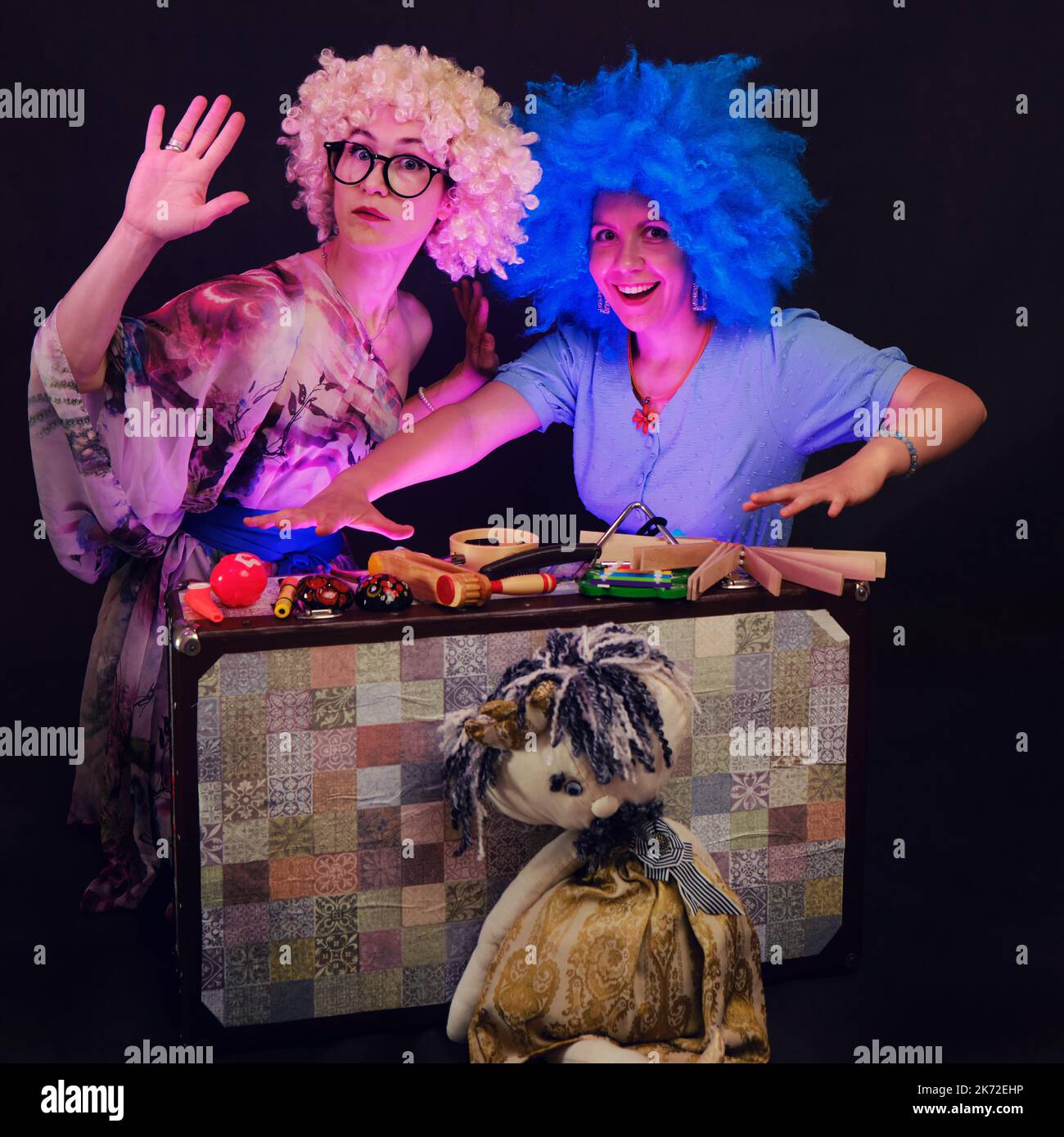 Happy women in funny wigs give a musical performance on a studio black ...
